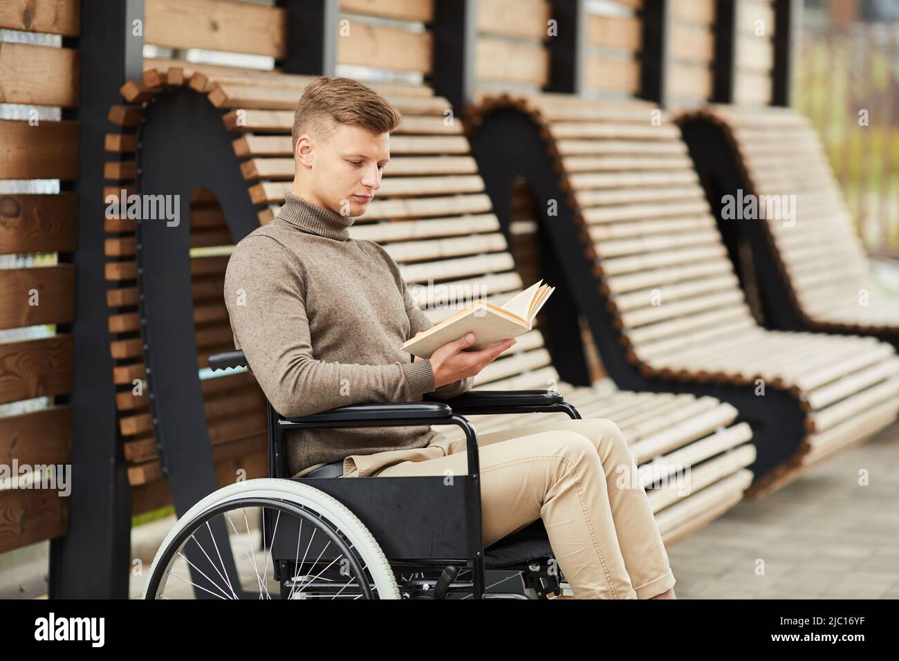 Concentrated young guy with hairstyle sitting in wheelchair at station ...
