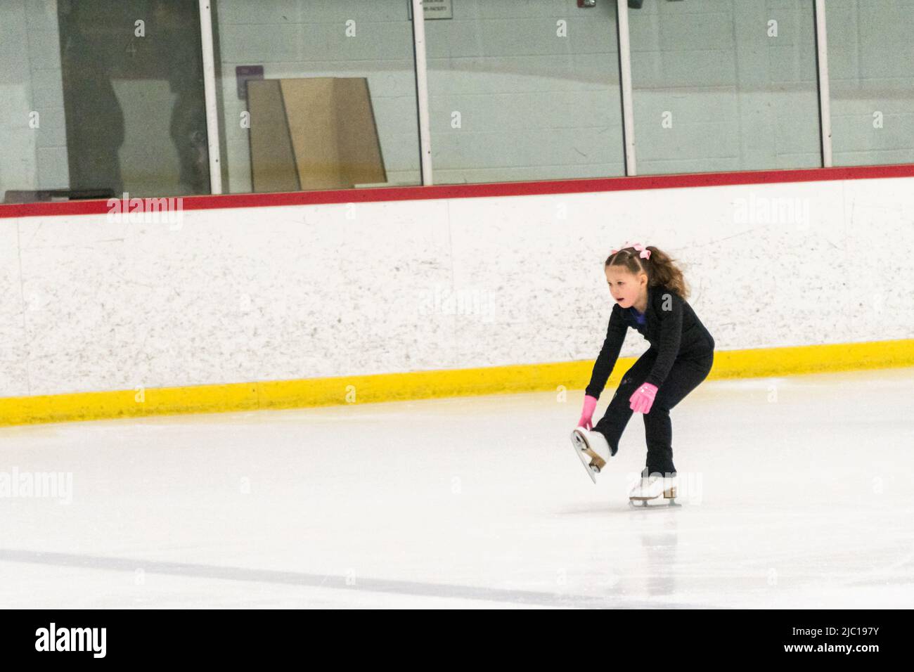 Little girl practicing figure skating moves on the indoor ice rink ...