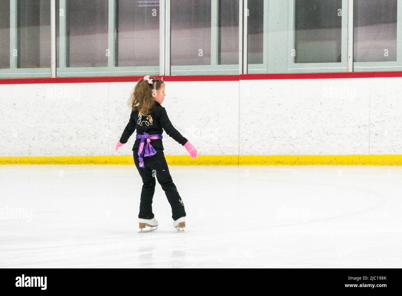 Little girl practicing figure skating moves on the indoor ice rink ...