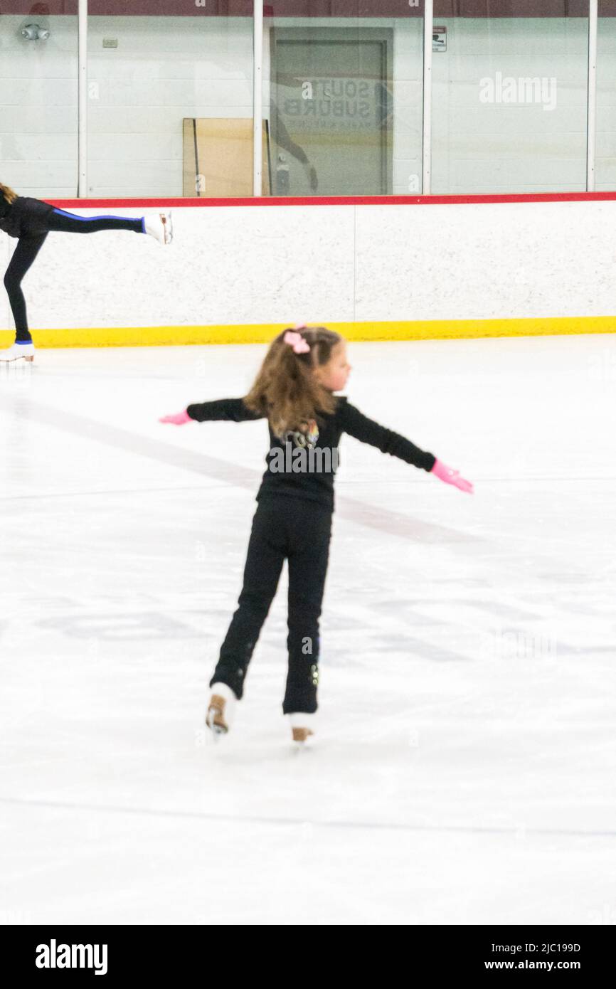 Little girl practicing figure skating moves on the indoor ice rink ...