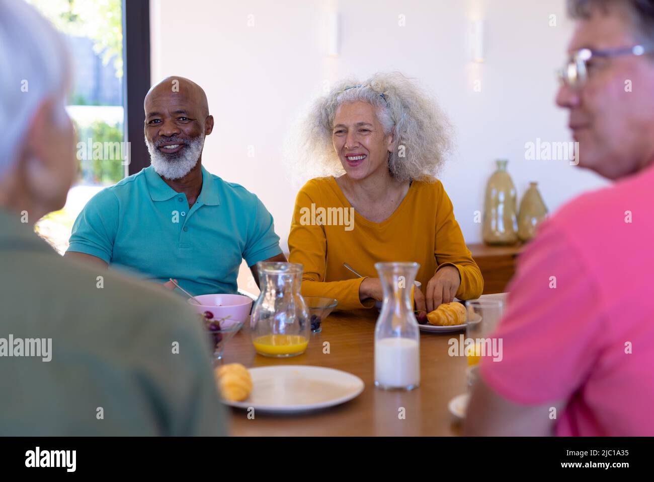 Happy multiracial senior friends talking while having breakfast at ...