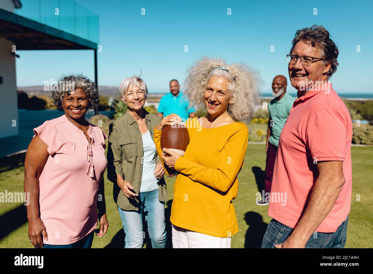 Portrait of happy multiracial senior friends playing rugby in yard ...