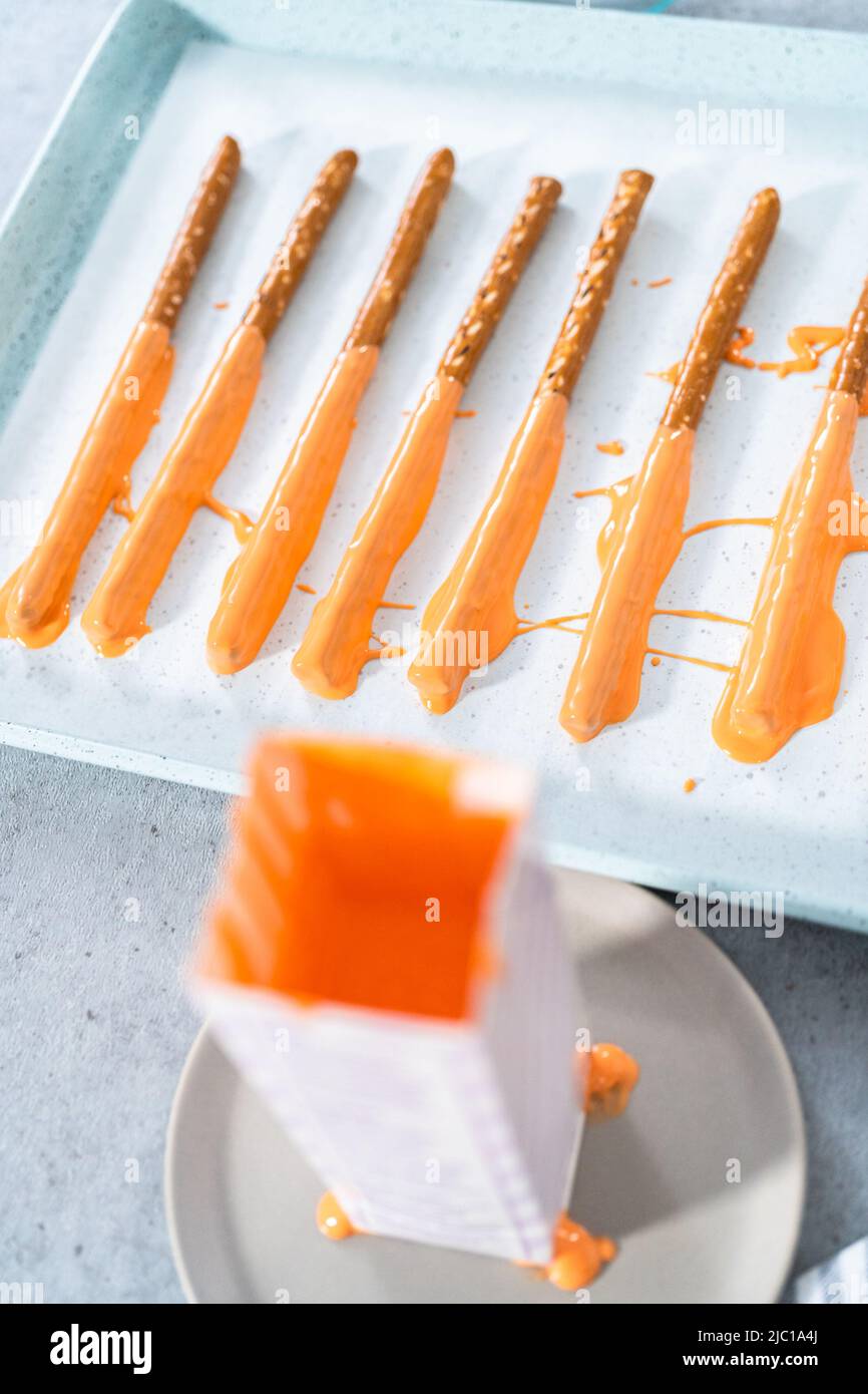 Dipping pretzel rods into melted chocolate to prepare carrot chocolate ...