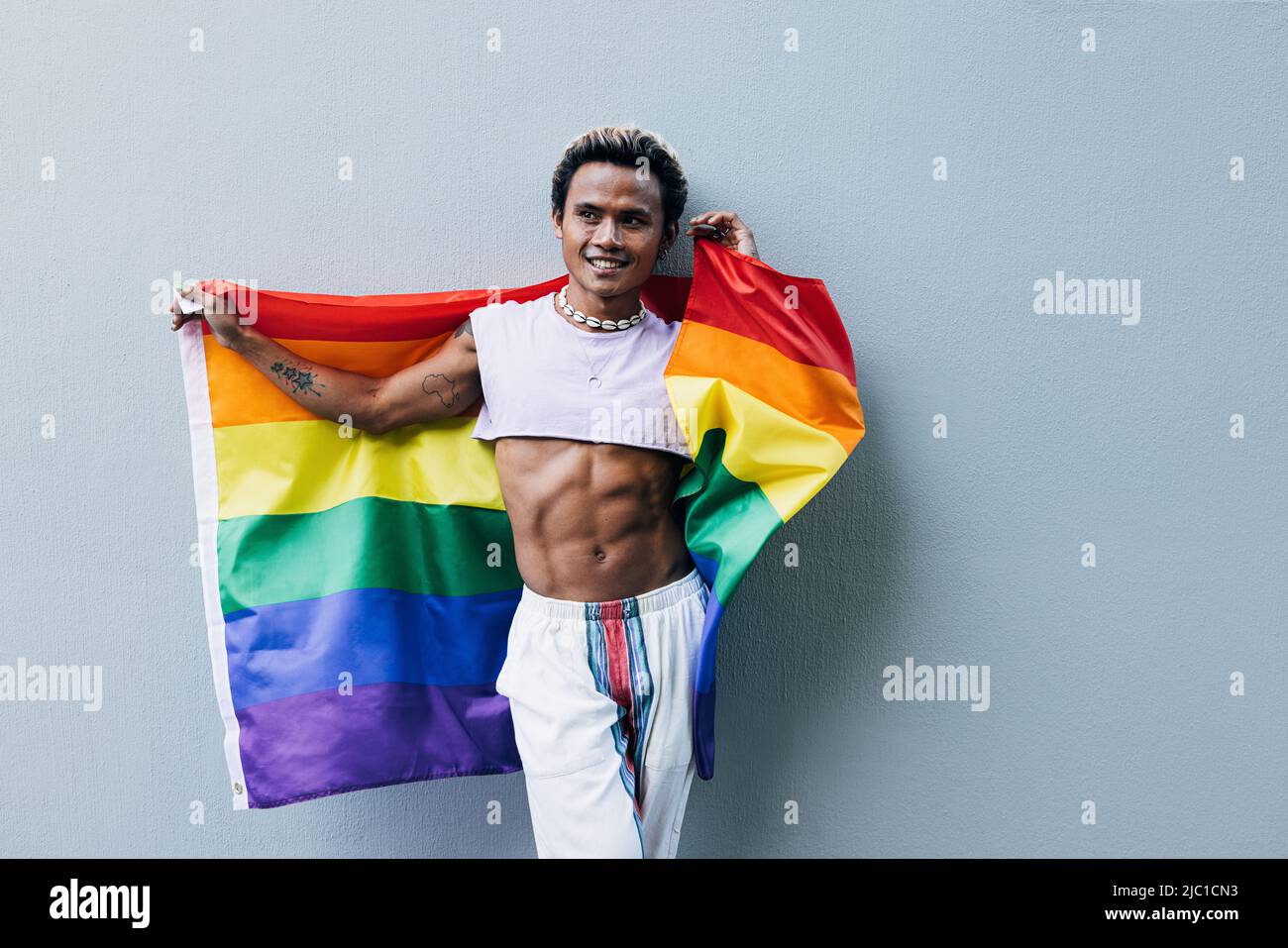 Smiling handsome guy holding rainbow flag outdoors Stock Photo - Alamy
