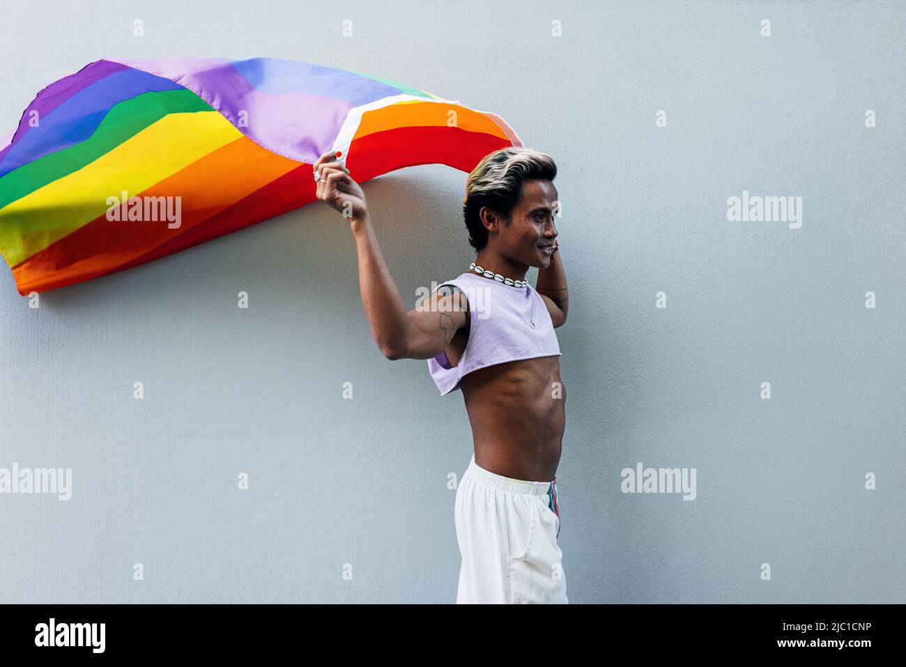 Stylish guy waving LGBT flag while walking at grey wall outdoors Stock ...