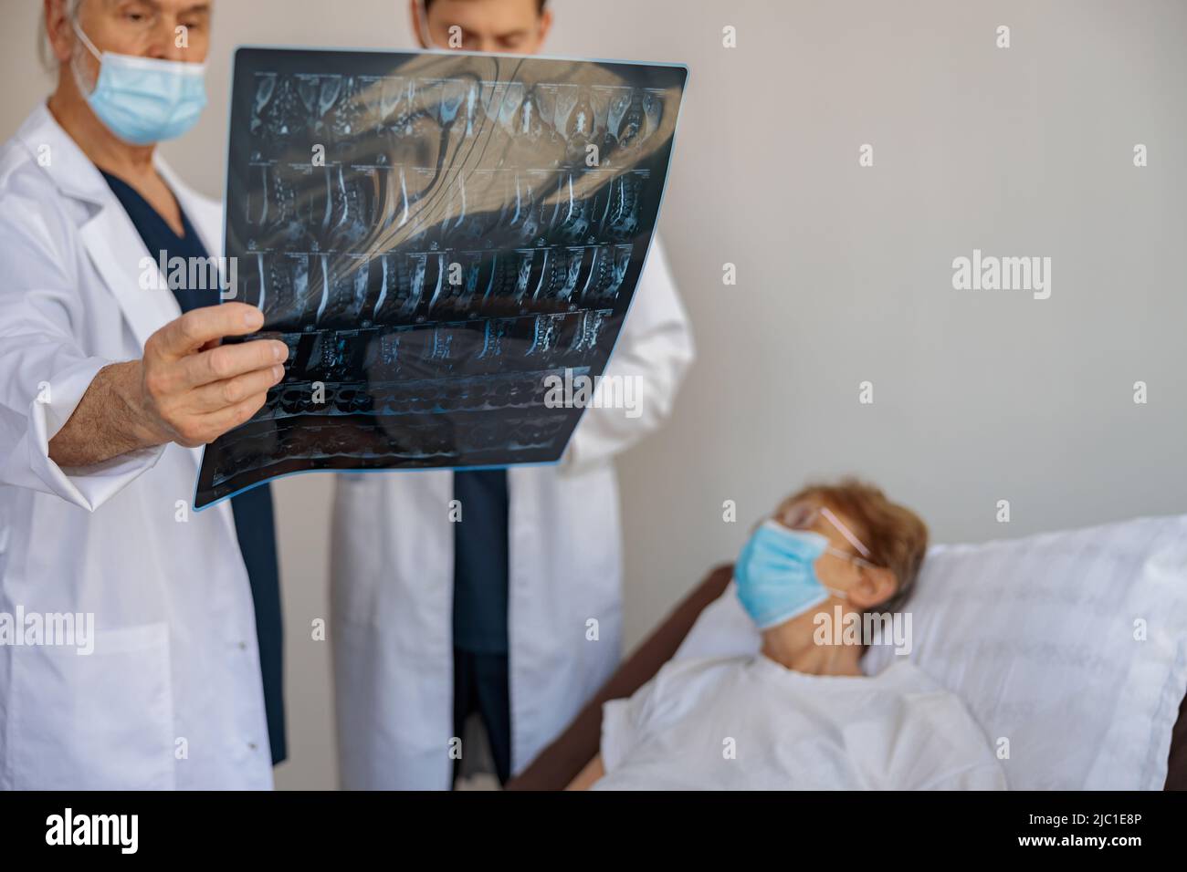 Two doctors in mask look and discuss an X-ray or MRI scan of the ...