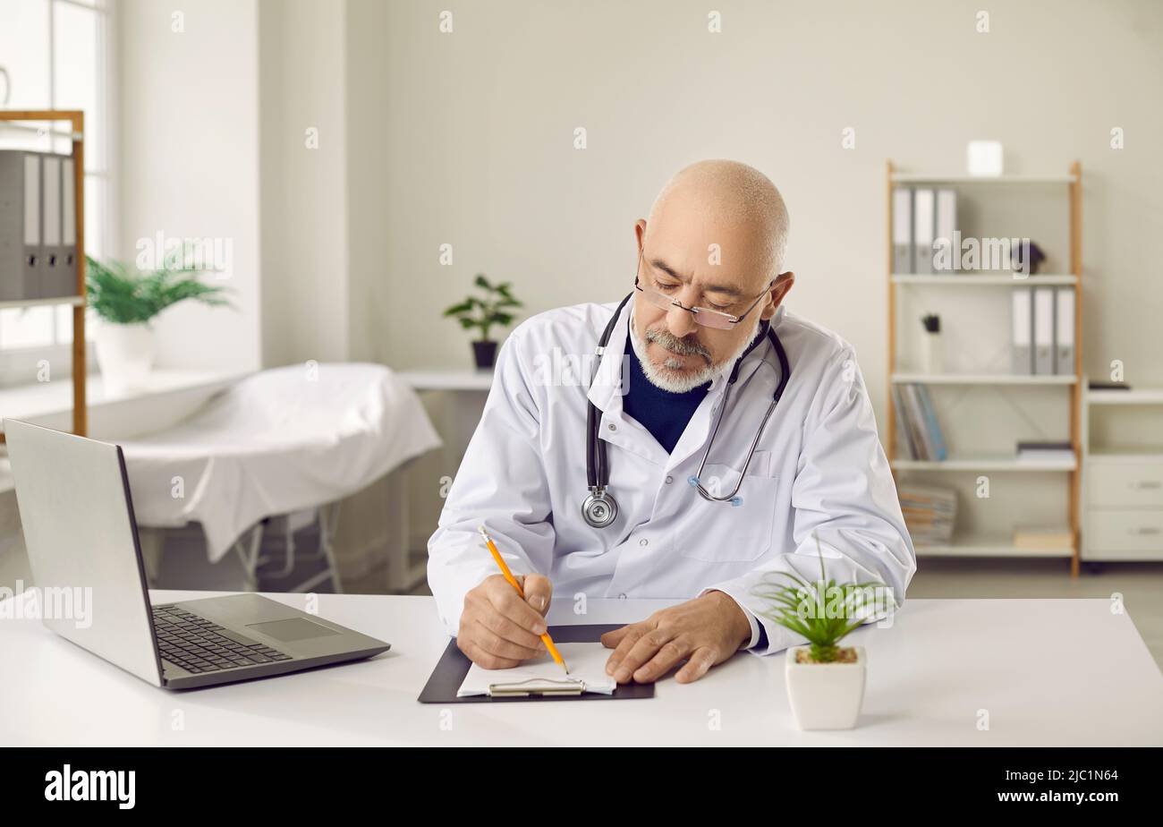 Old doctor in glasses write prescription work on computer Stock Photo ...