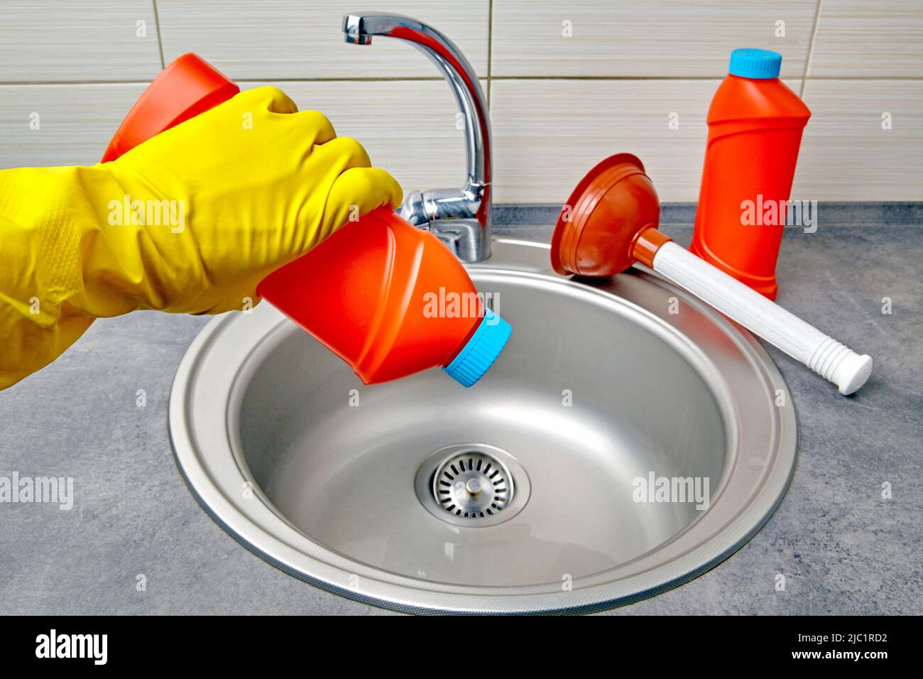 Hands in yellow rubber gloves hold a plunger and a pipe cleaner against ...