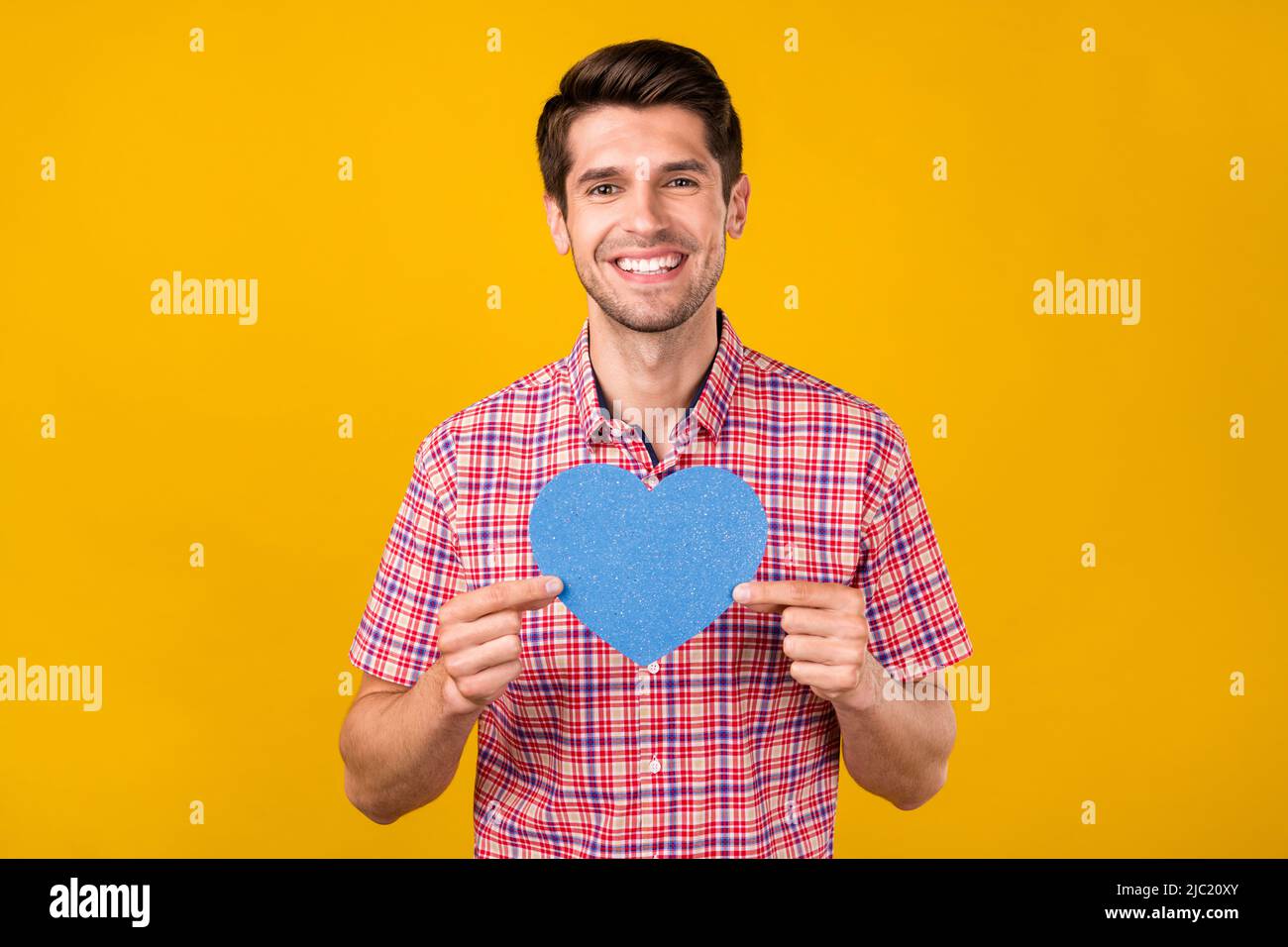 Portrait of attractive cheerful guy holding blue card heart affection ...