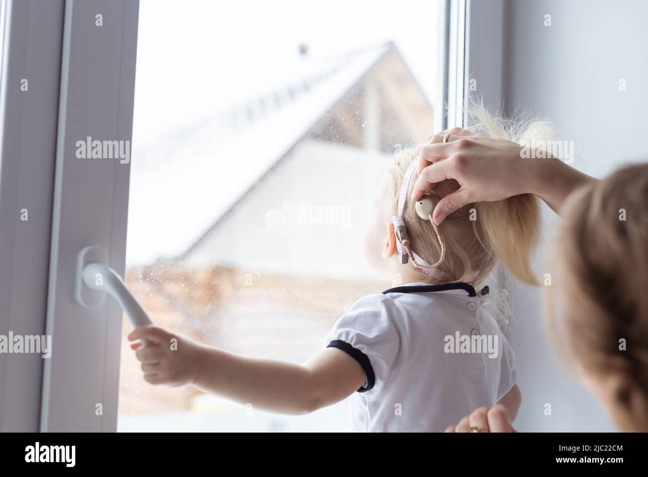 Mother helps her deaf baby daughter putting hearing aid in little girl ...