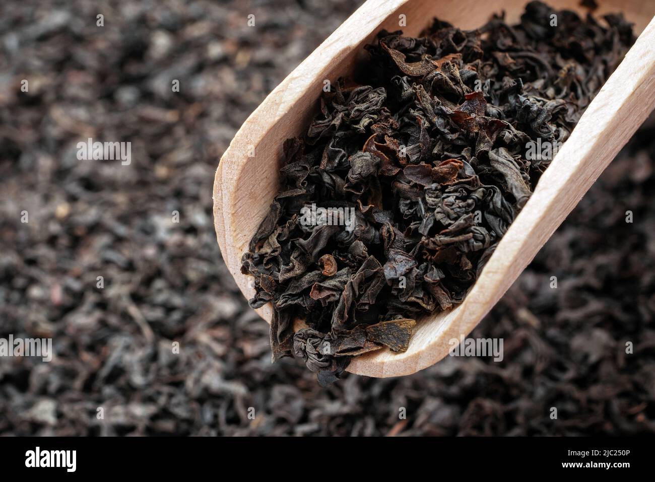 Dry long leaf tea in wooden scoop. Macro of loose black tea Stock Photo ...