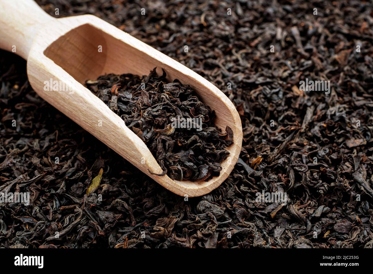 Dry long leaf tea in wooden scoop. Macro of loose black tea Stock Photo ...
