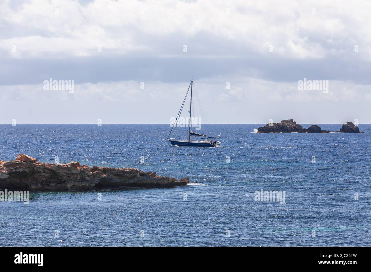 Sailing boat without sails maneuvers between rocks protruding above ...