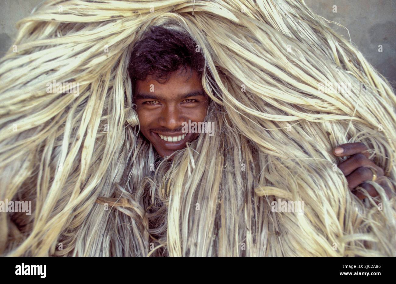 Bangladesh; portrait of a smiling man covered with strands of jute that ...