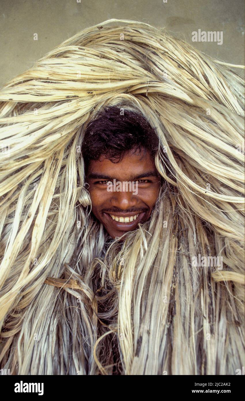 Bangladesh; portrait of a smiling man covered with strands of jute that ...
