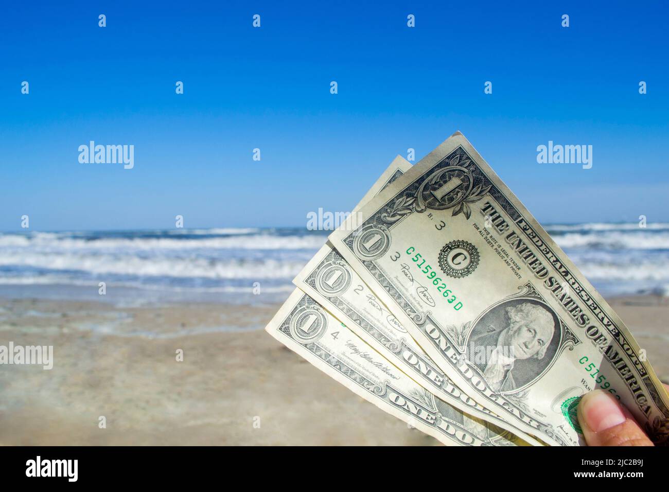 Person holding three paper dollar bills on background of sea and sea ...