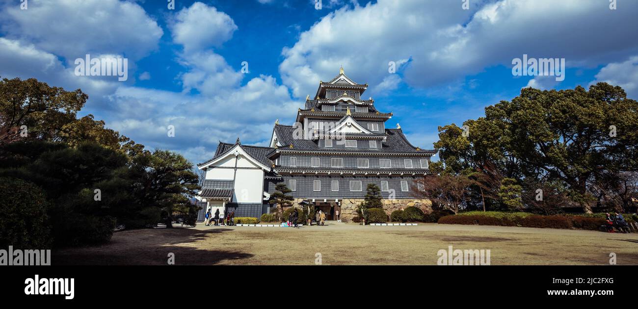 View to the Japanese Okayama Castle through the trees under Blue Cloudy ...