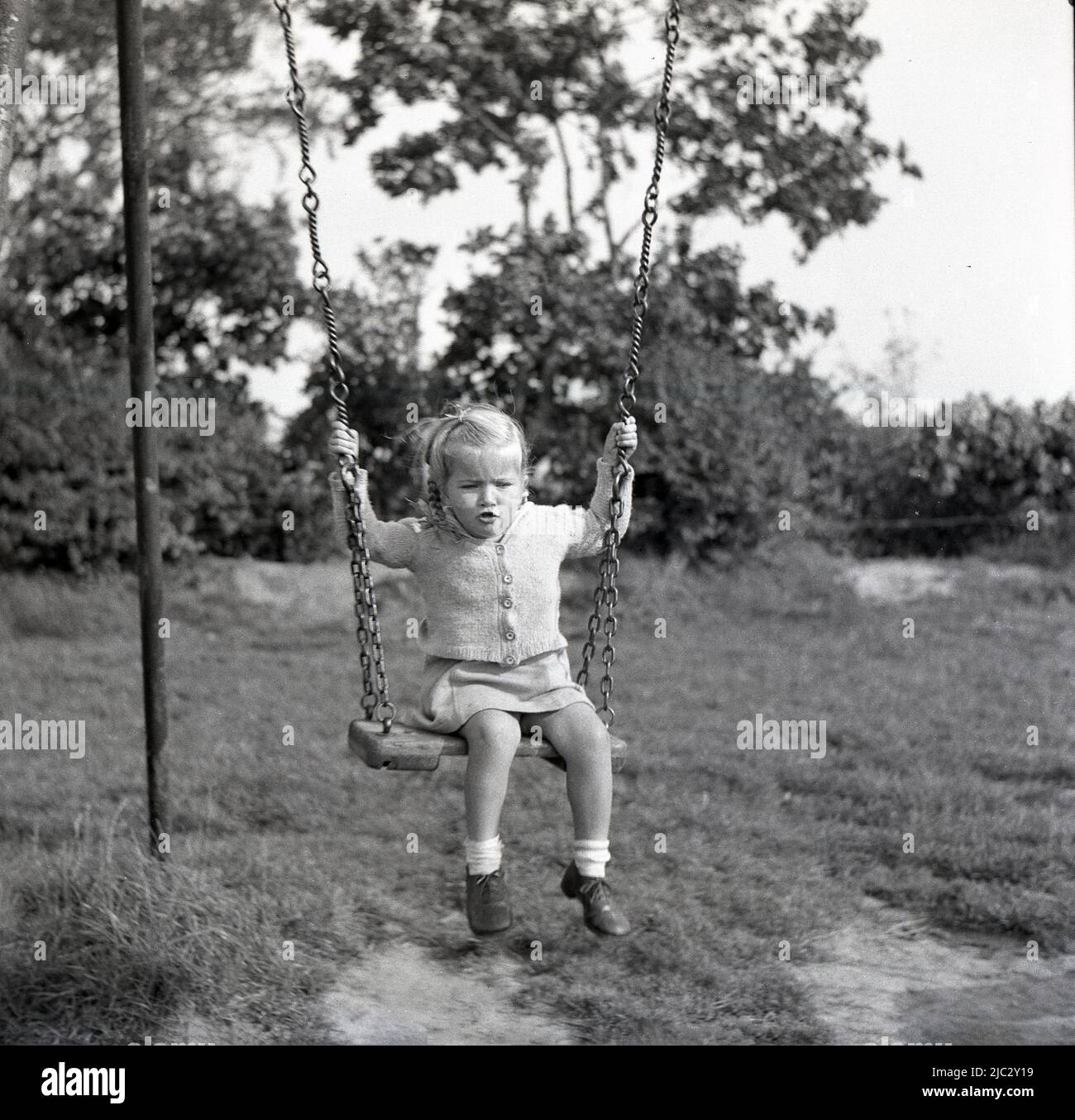 1950s, historical, outside in a countryside playground, a little girl ...