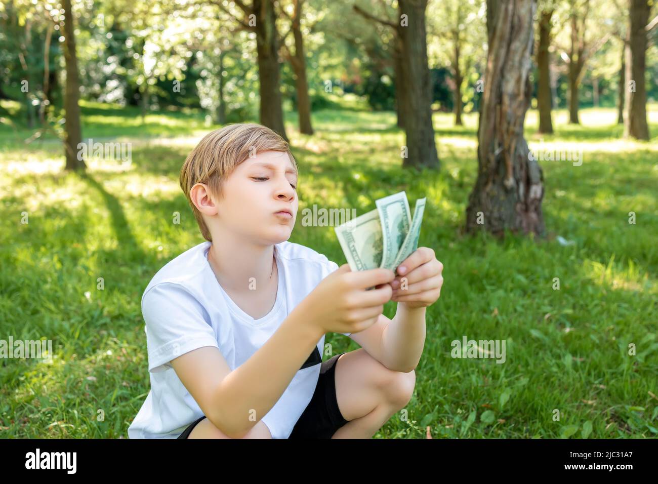 the boy is squatting in the park, counting banknotes and grimacing ...