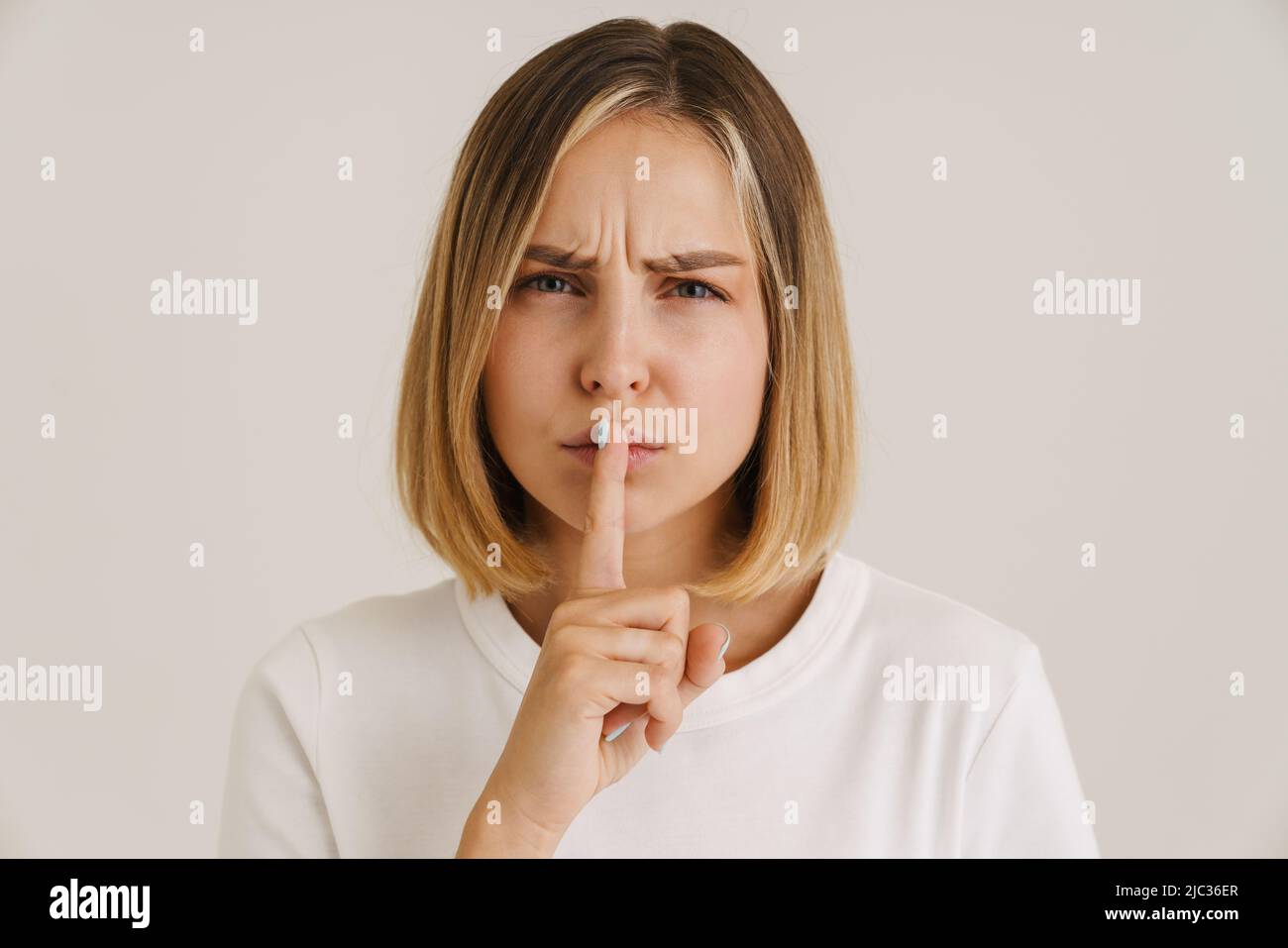 Young blonde woman frowning while showing silence gesture isolated over ...