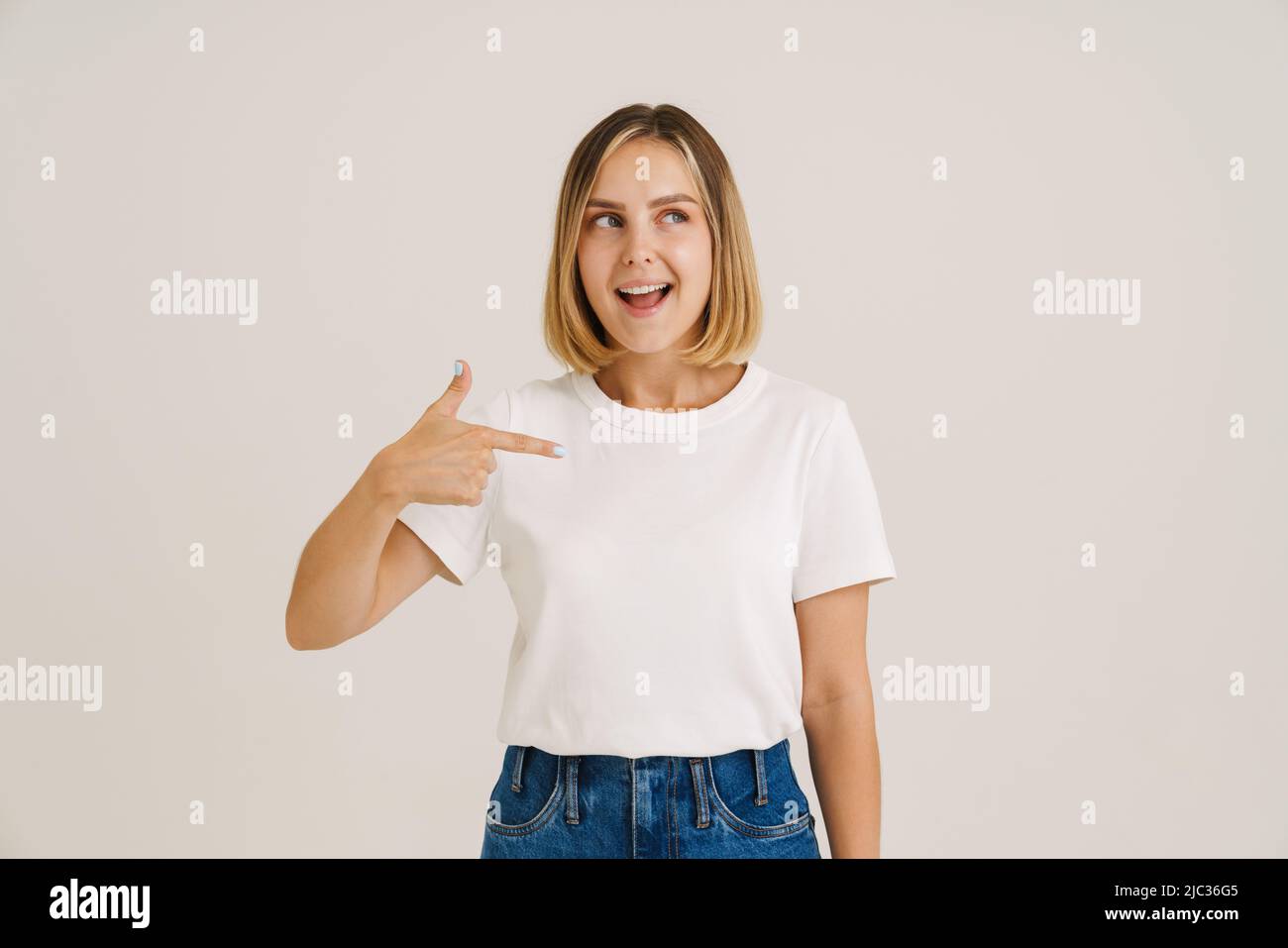 Young excited woman smiling while pointing finger aside isolated over ...