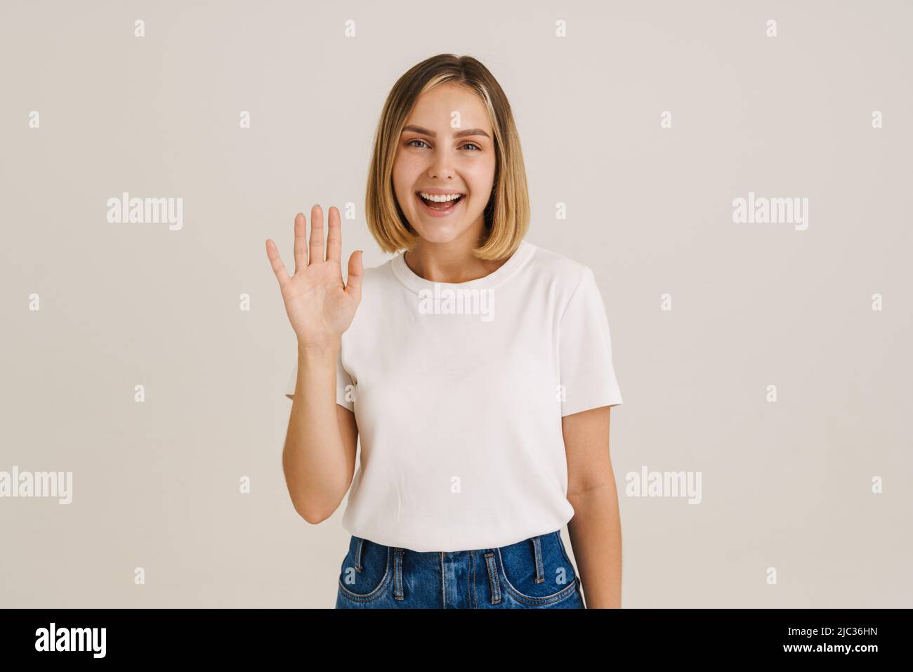 Young blonde woman smiling while waving hand at camera isolated over ...