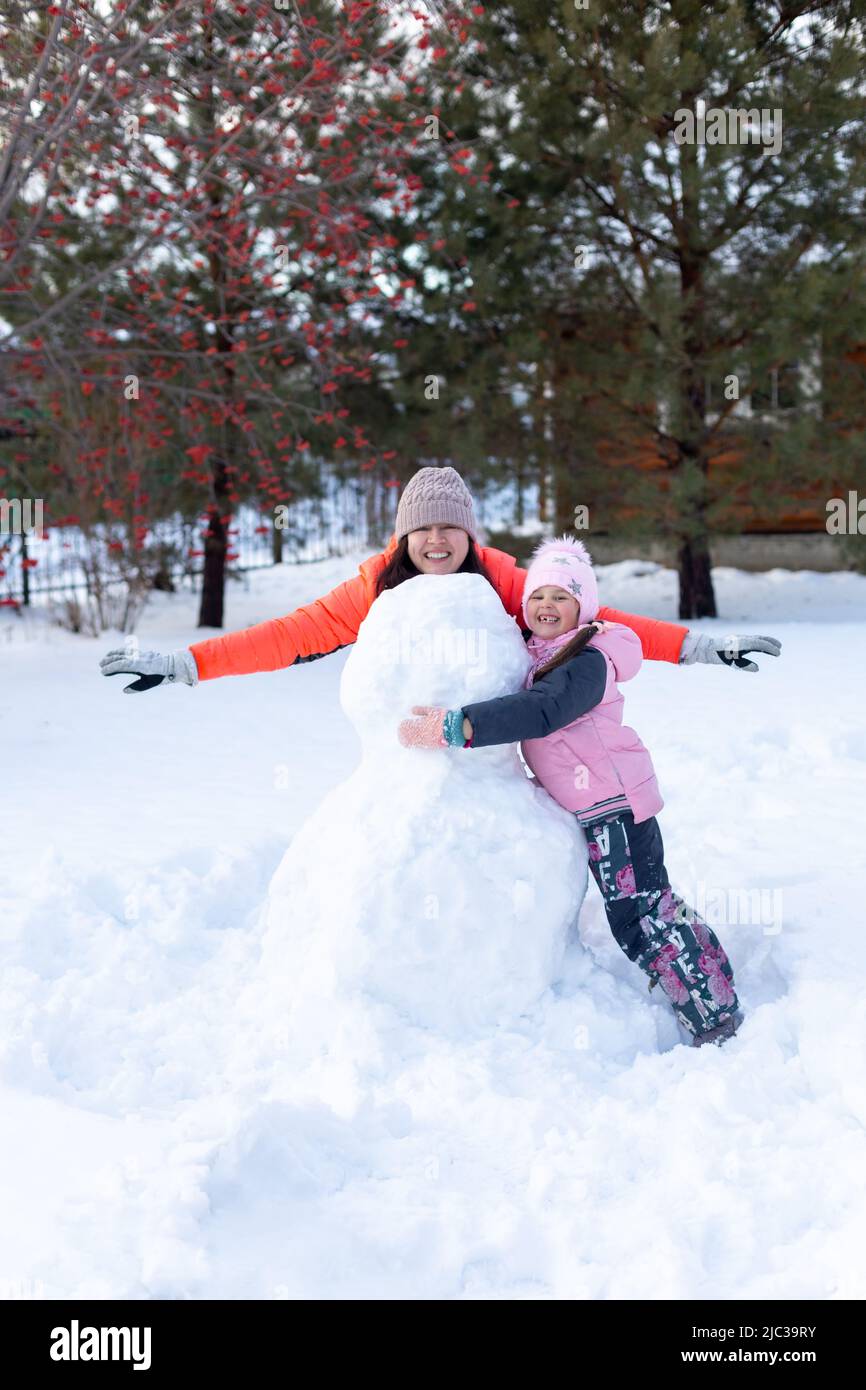 Woman with hands half raised standing on snow behind unfinished snowman ...