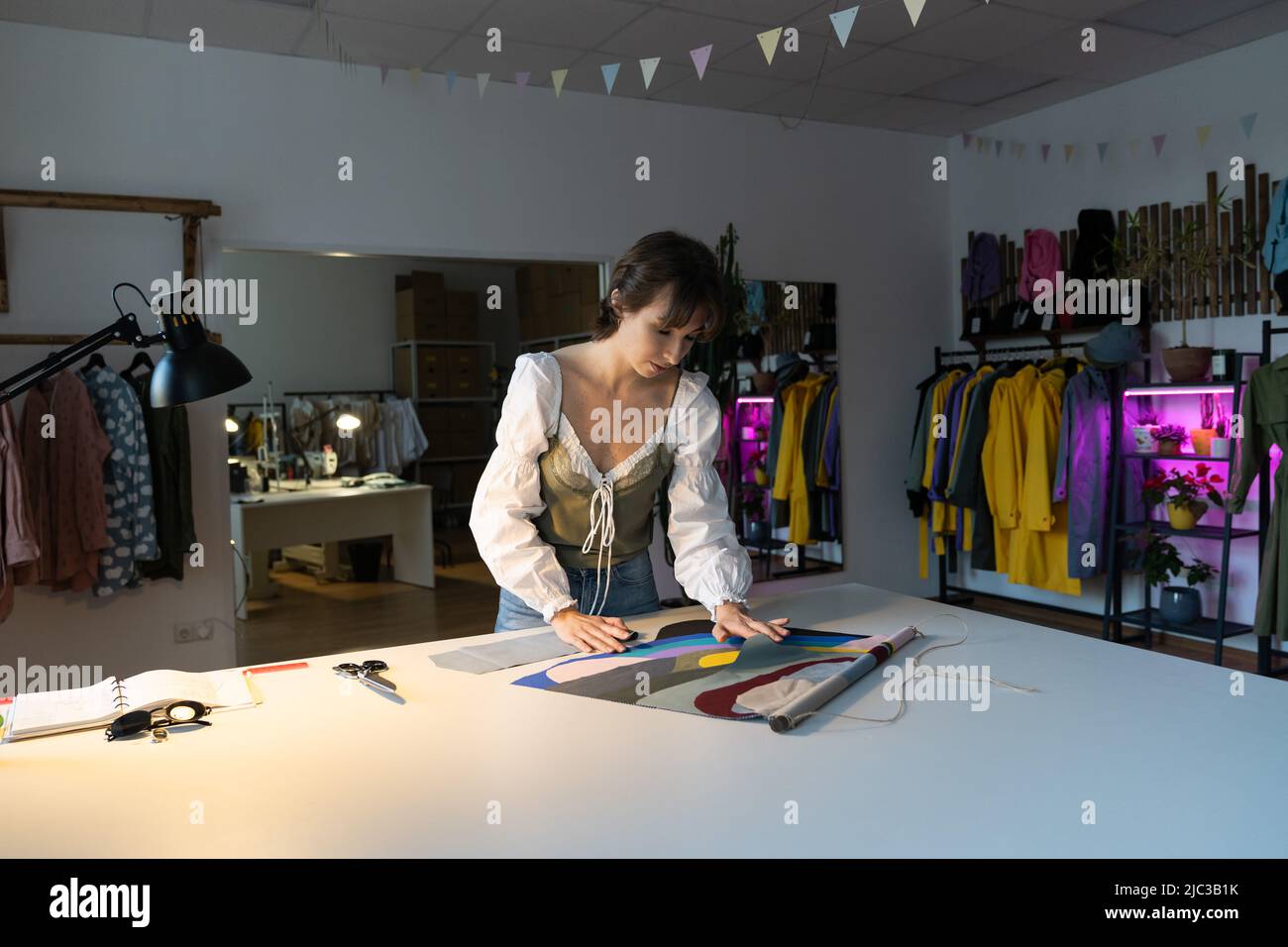 Woman fashion designer work late in workshop choosing textile samples ...