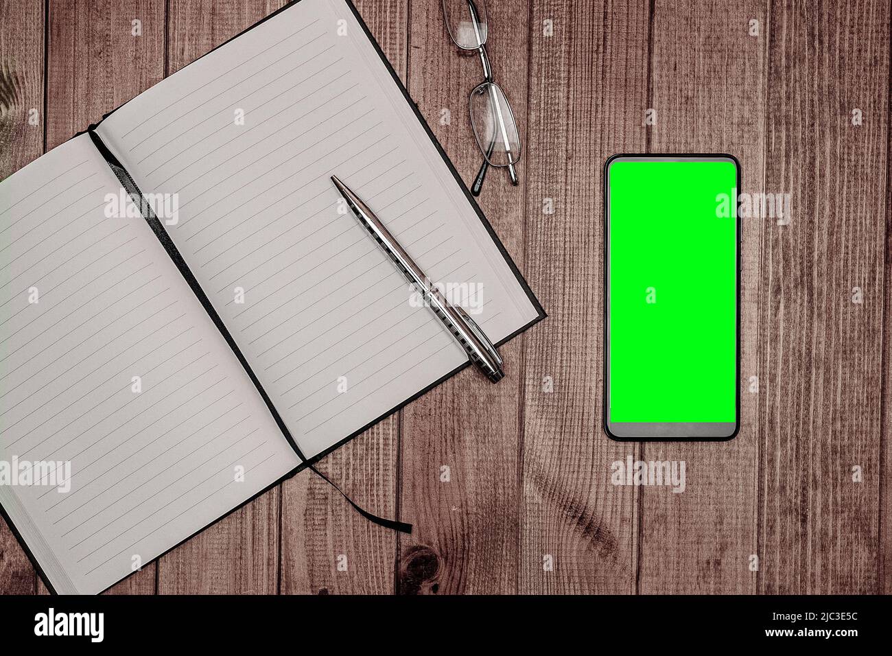 mobile phone with a green screen, a notepad and a pen on the background ...