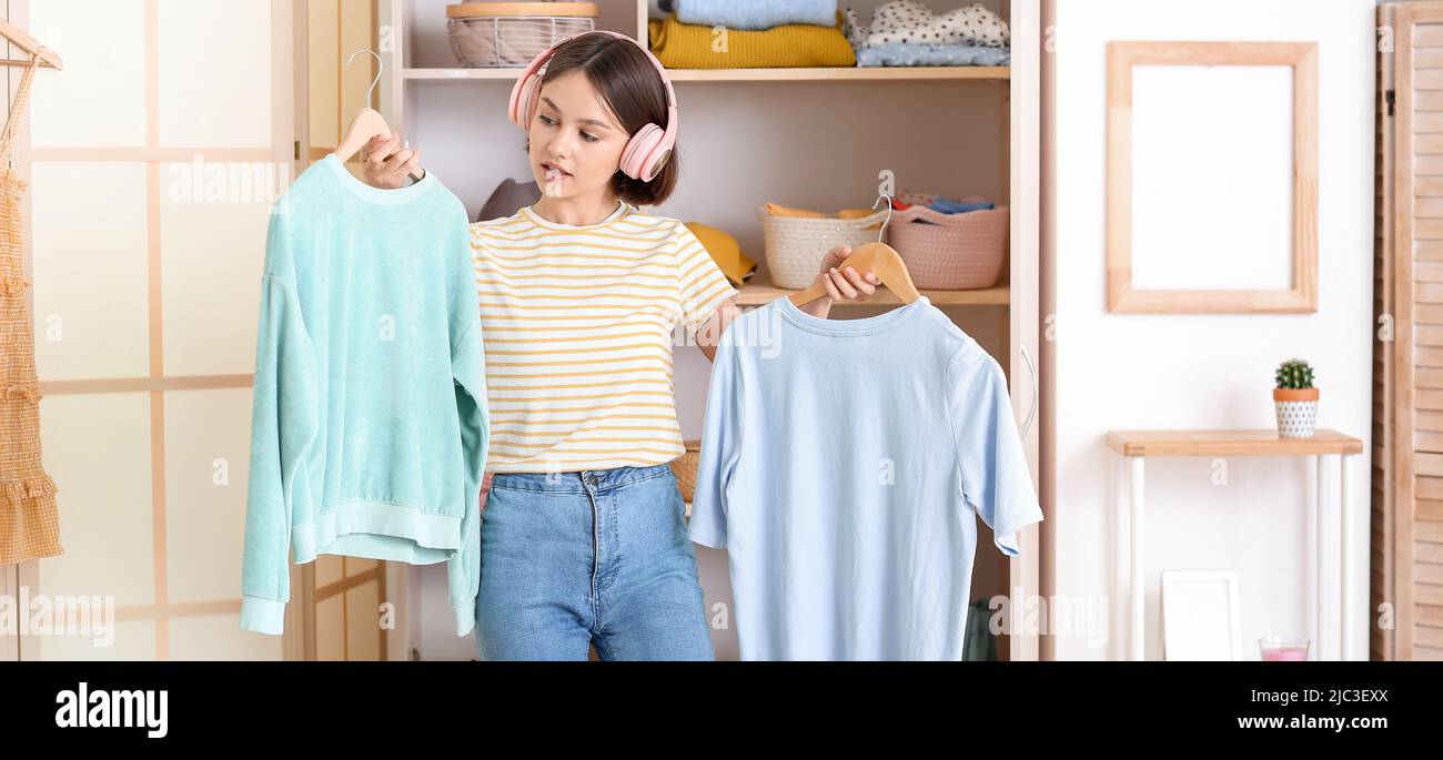 Young woman listening to music while choosing clothes in dressing room ...