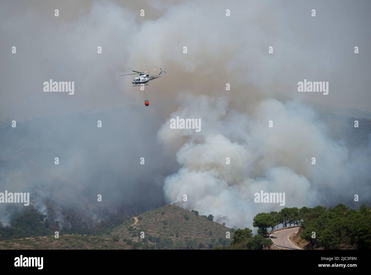 General view of smoke rising over the mountains as a helicopter flies ...