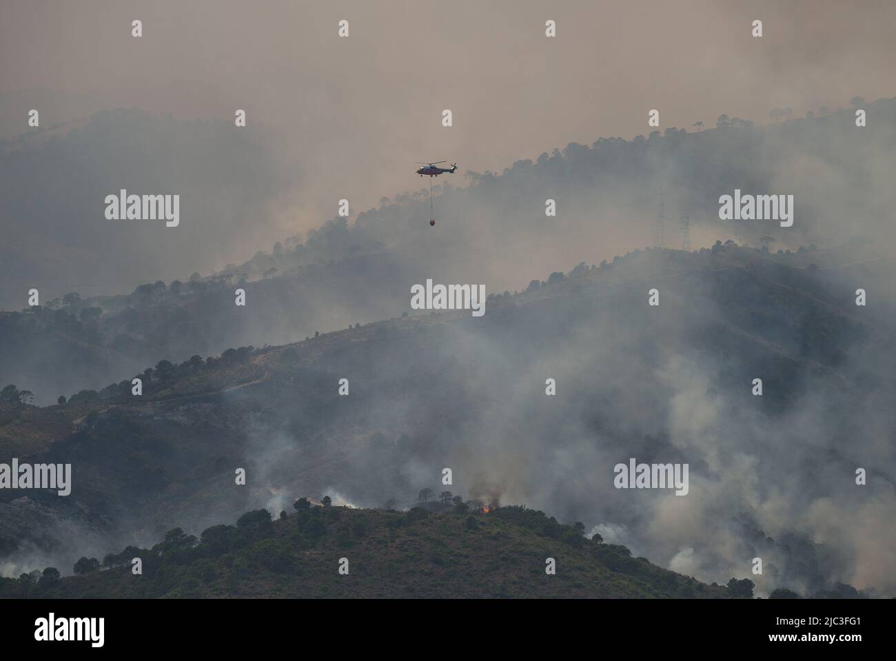 General view of smoke rising over the mountains as a helicopter flies ...