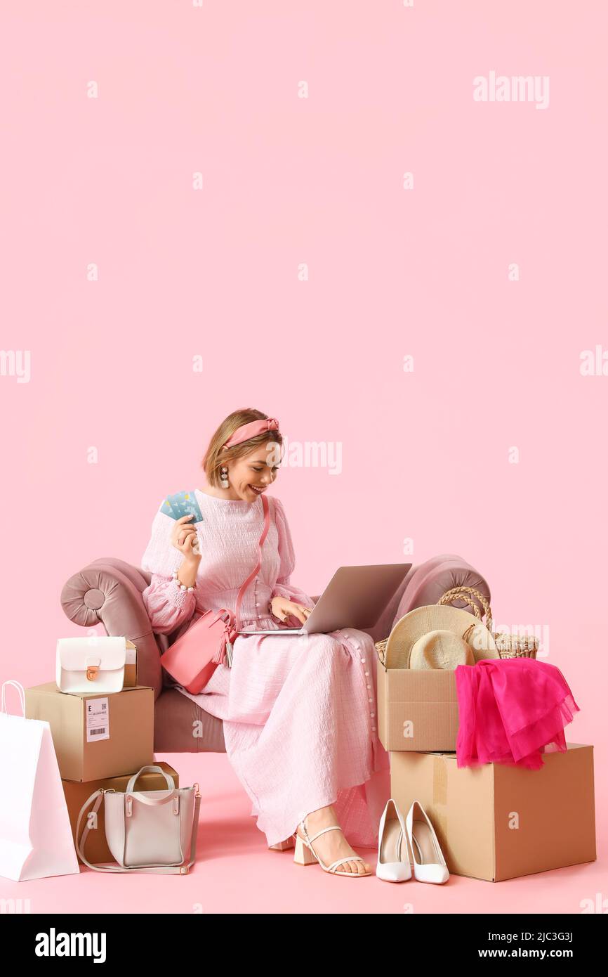 Young woman with credit card and laptop on pink background. Online ...