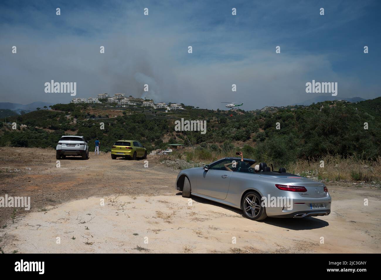 A woman in a car takes photos of the smoke rising over the mountains ...
