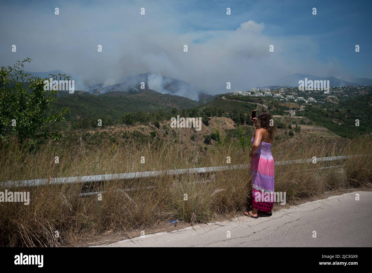 A woman takes photos of the smoke rising over the mountains during a ...