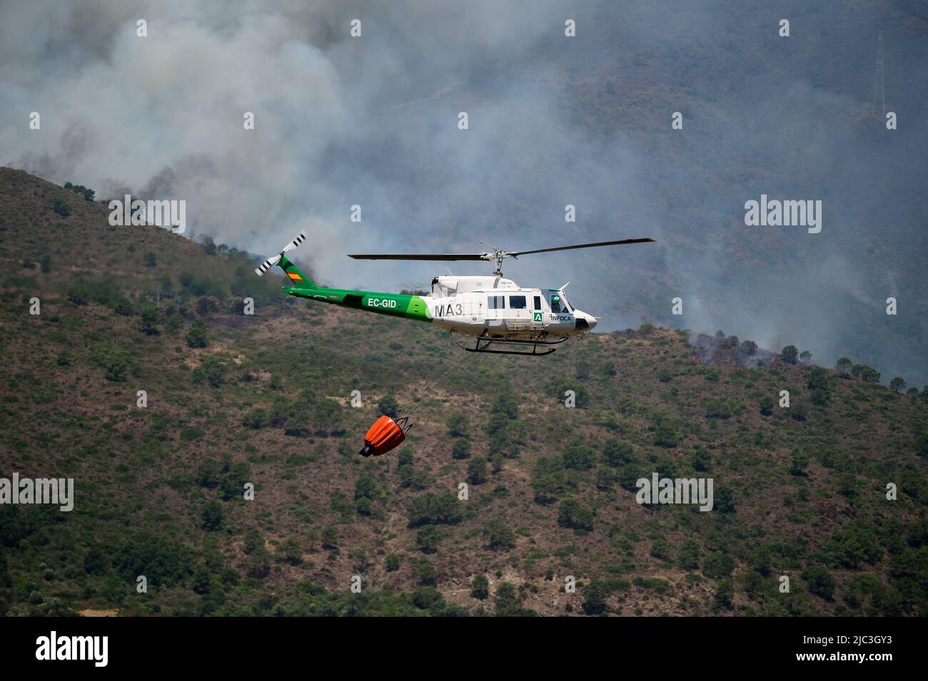 General view of smoke rising over the mountains as a helicopter flies ...