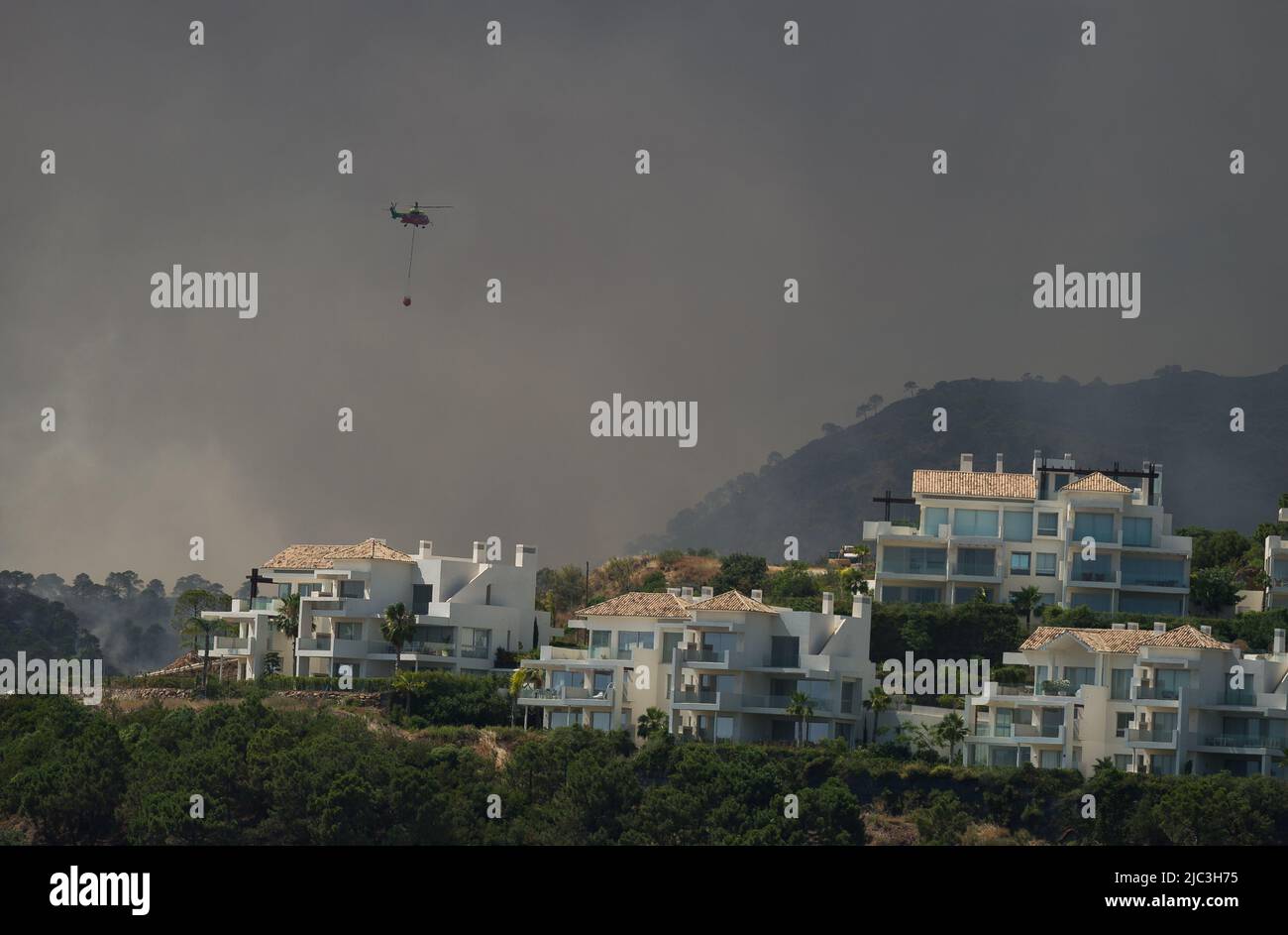 General view of smoke rising over the mountains as a helicopter flies ...