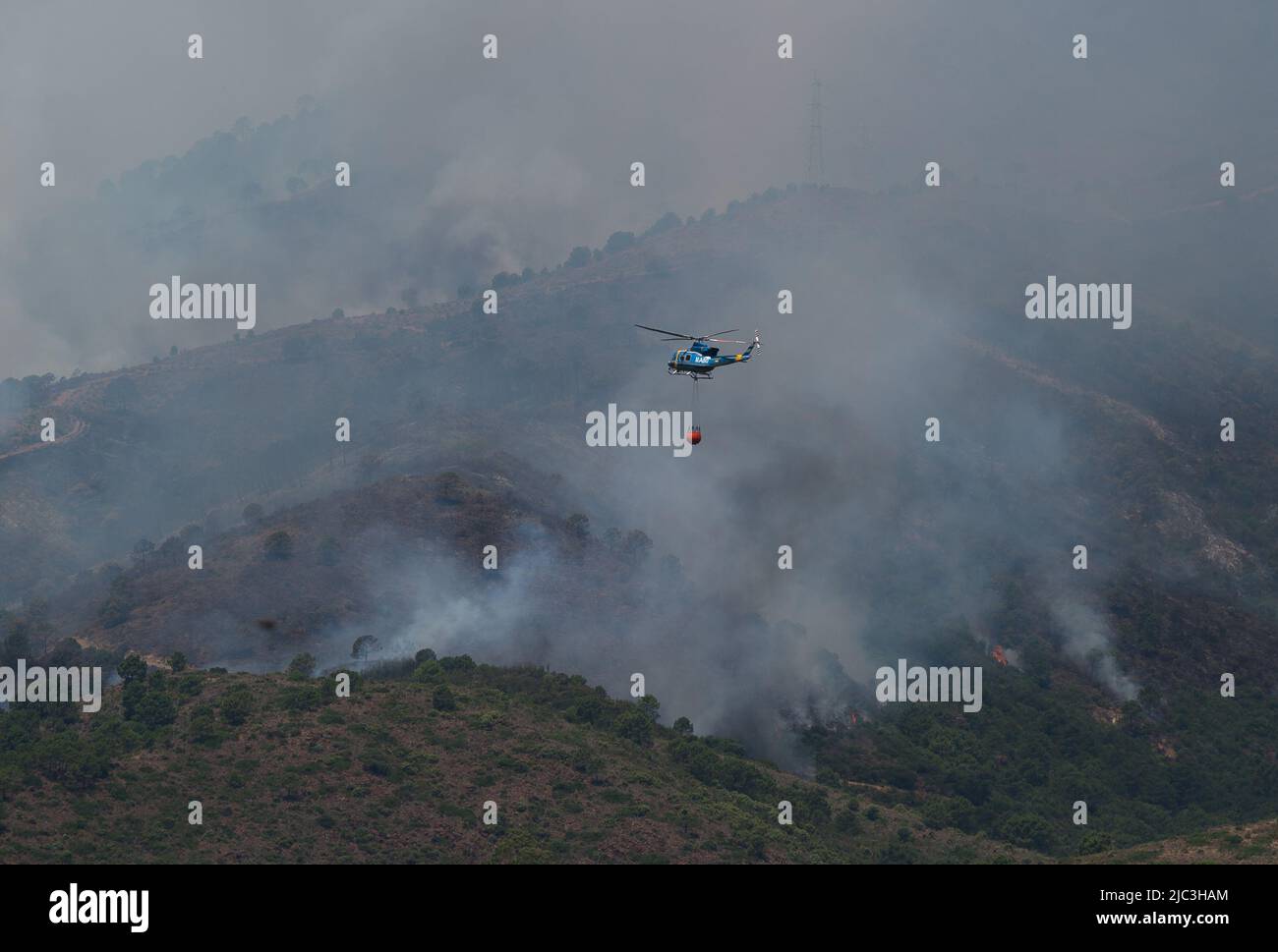General view of smoke rising over the mountains as a helicopter flies ...