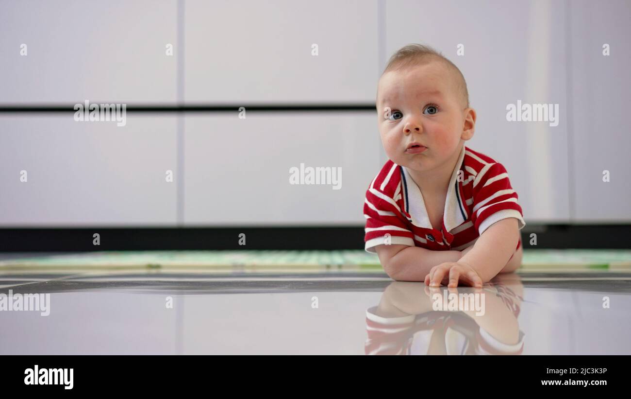 A little boy learns to crawl on tiles in the kitchen. A small child ...