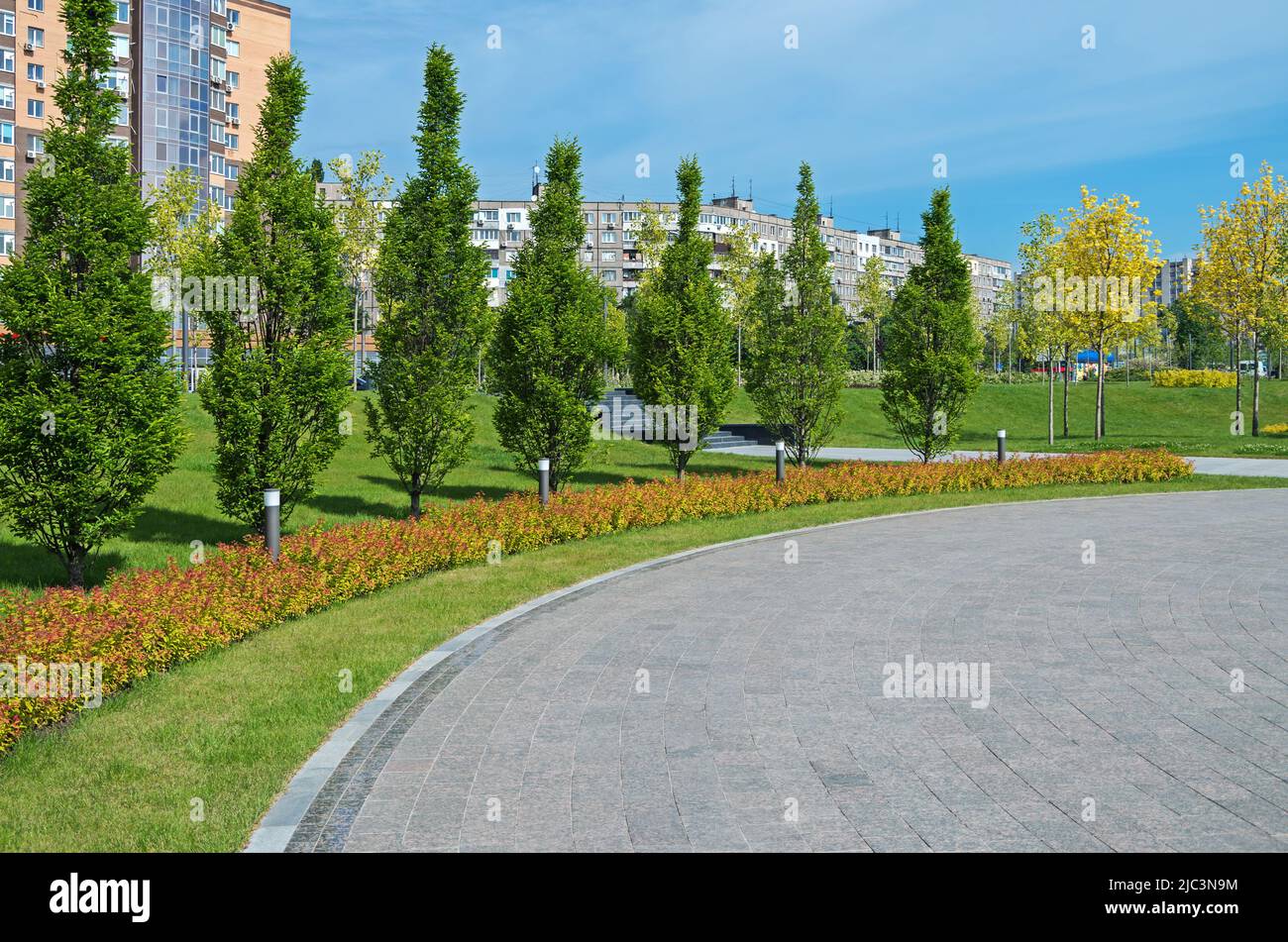 Granite footpath bends around red ornamental bushes and young green ...