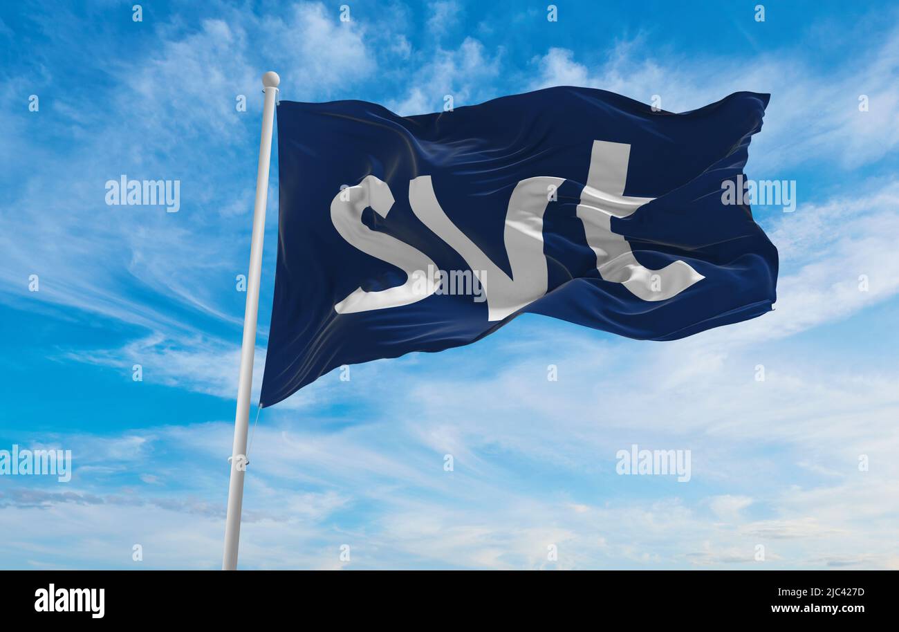 official flag of SVT , Sweden at cloudy sky background on sunset ...