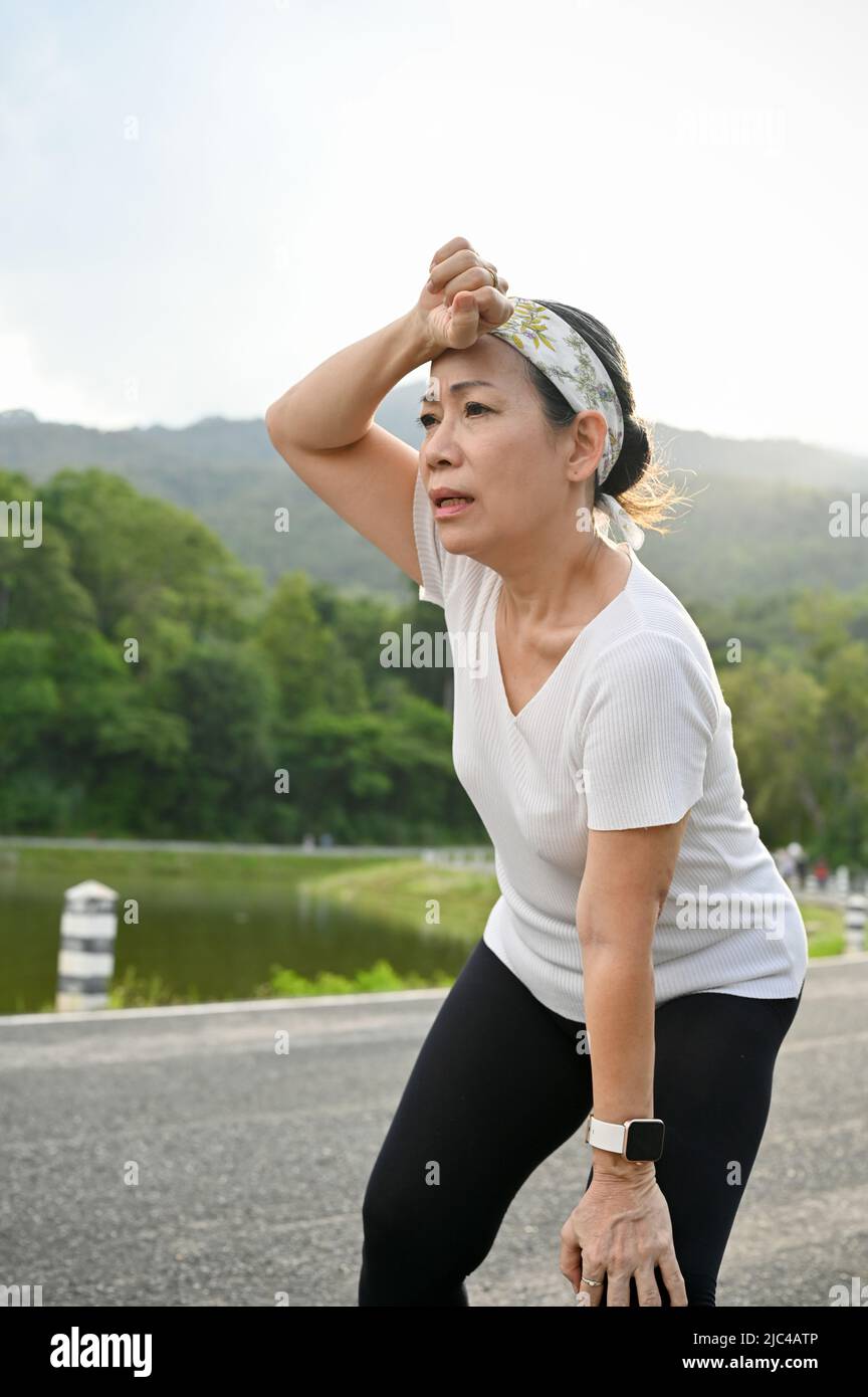 Exhausted asian aged woman taking a break after had a long jogging in ...