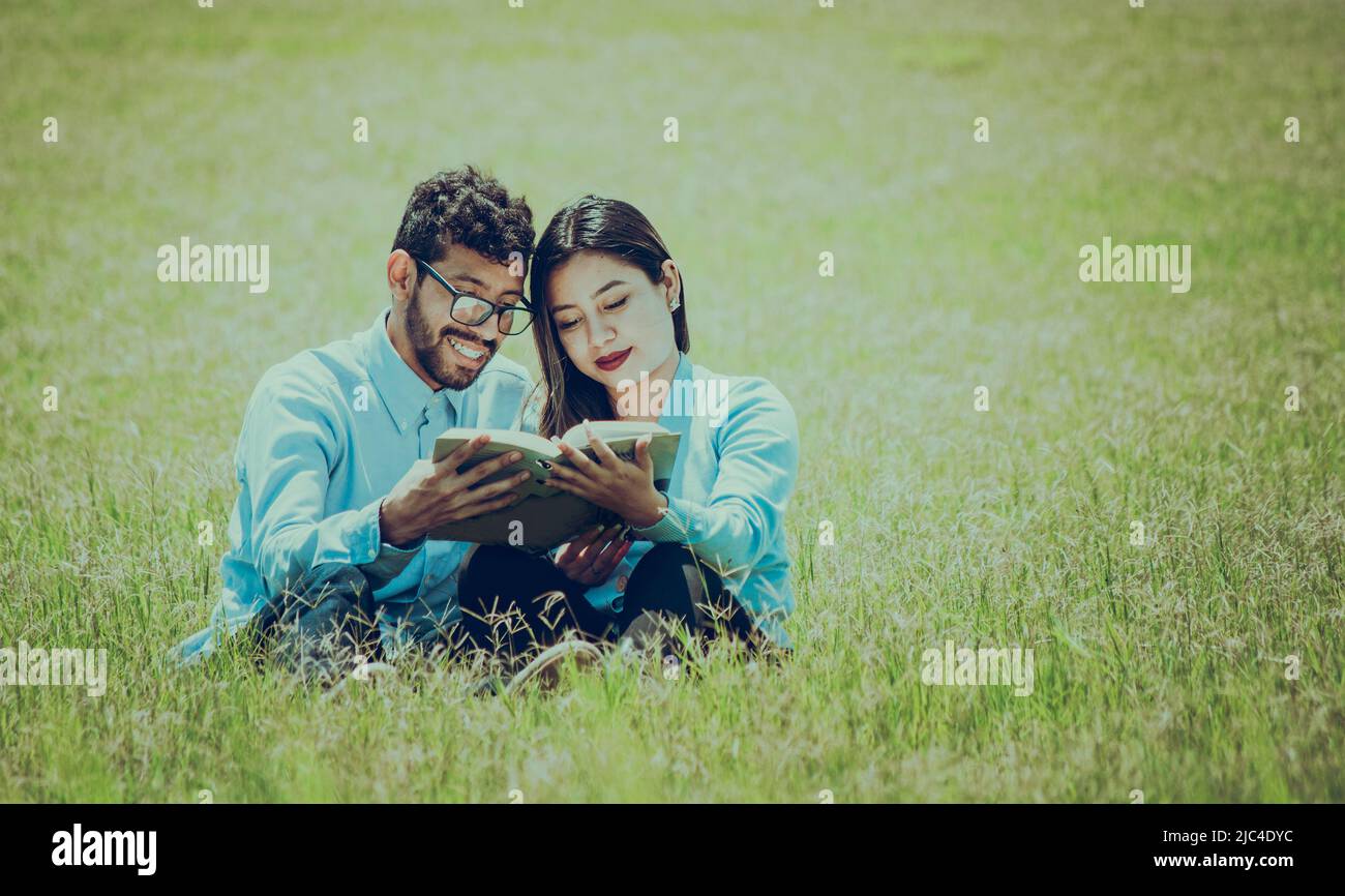 Two people sitting on the grass reading a book, concept of people ...