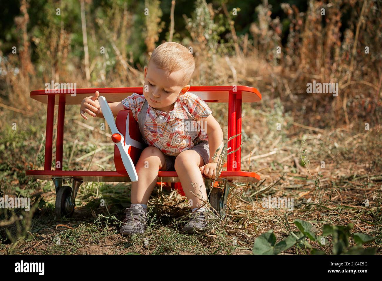 Happy kid boy pilot sitting and playing with toy red airplane on summer ...