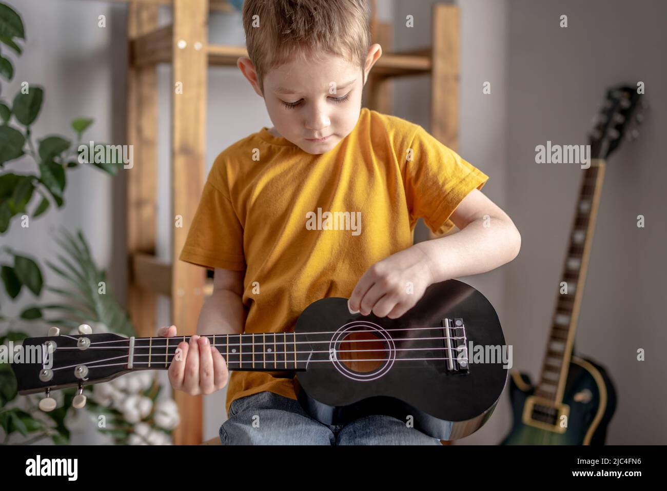 Cute funny boy is playing ukulele guitar in the music room. Joyful ...