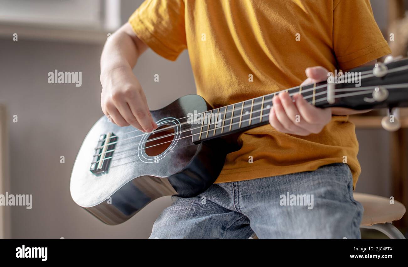 Cute funny boy is playing ukulele guitar in the music room. Joyful ...