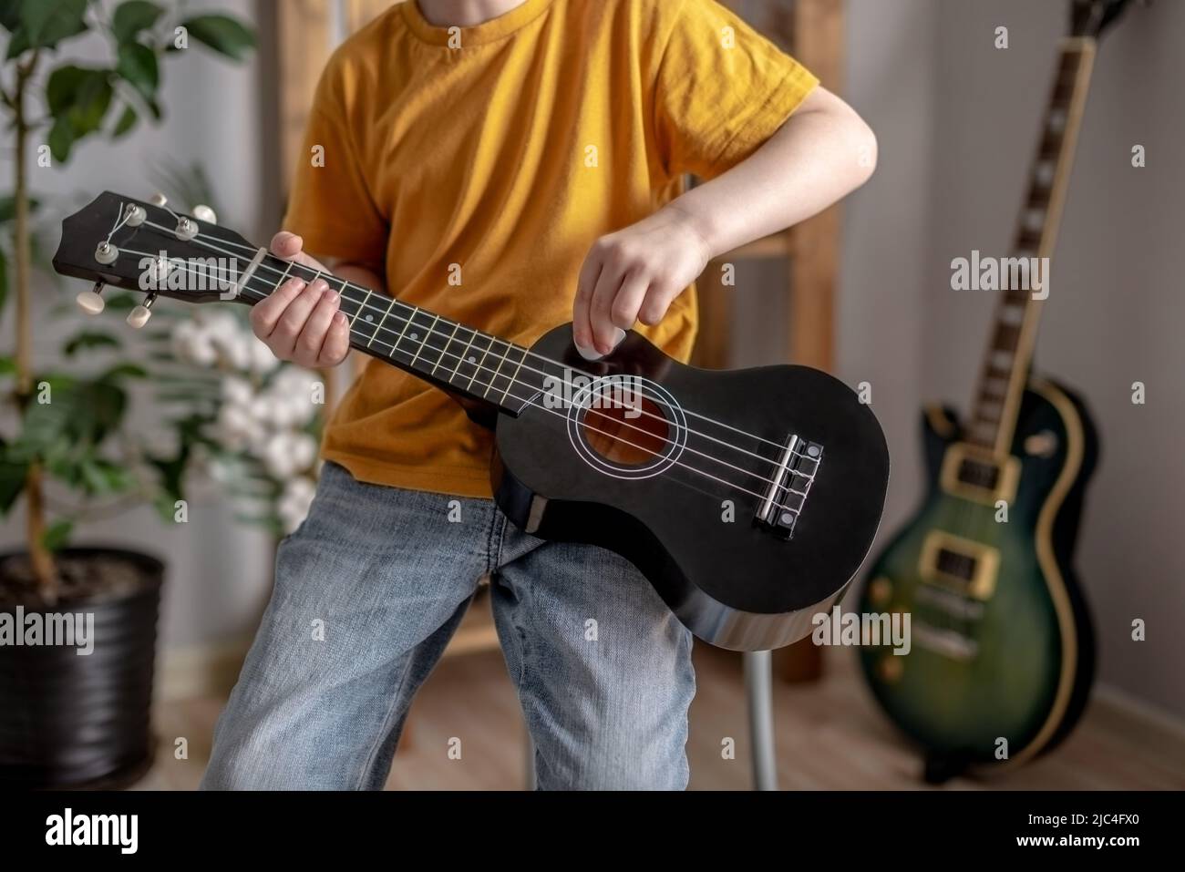 Cute funny boy is playing ukulele guitar in the music room. Joyful ...
