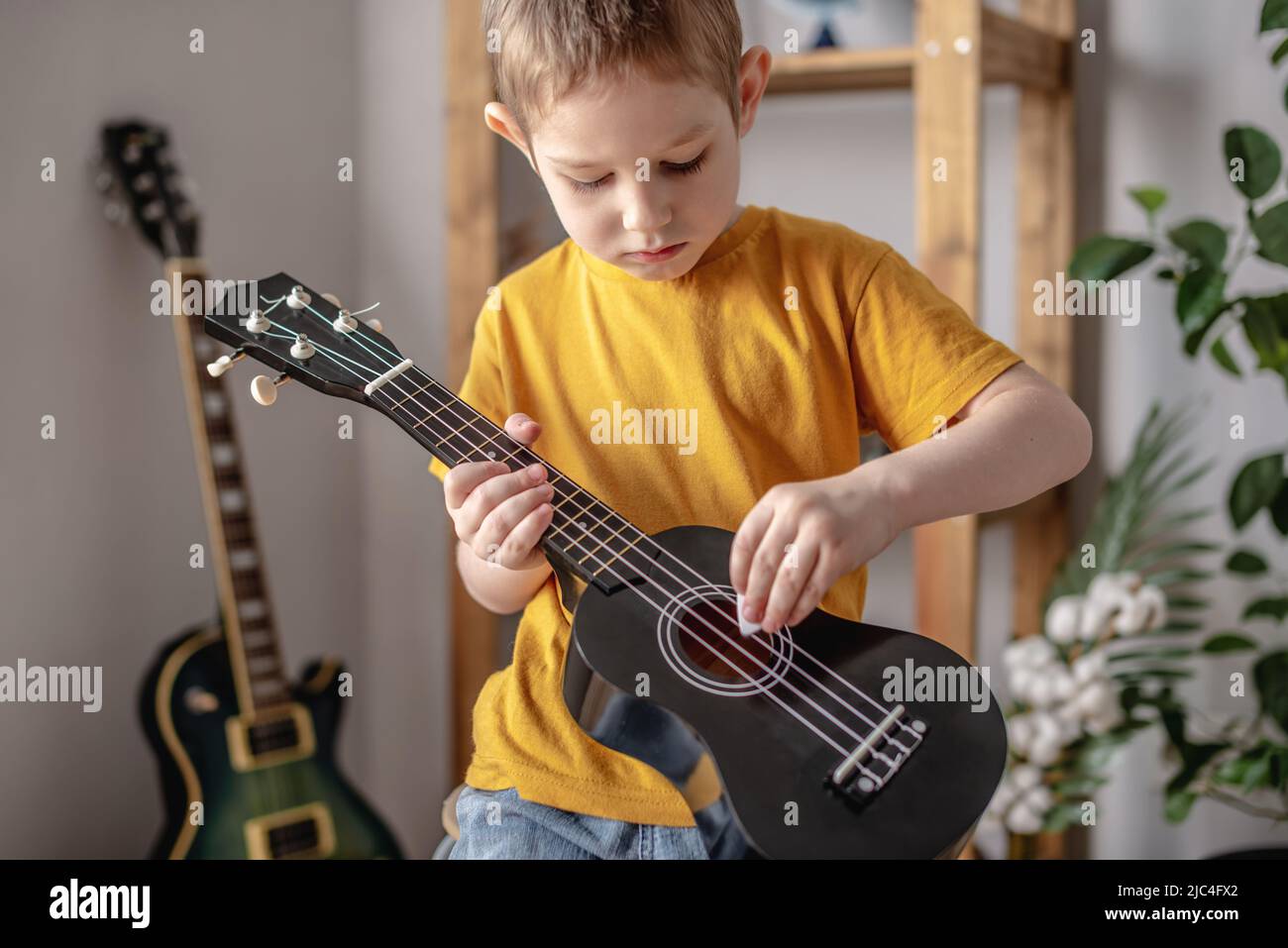 Cute funny boy is playing ukulele guitar in the music room. Joyful ...