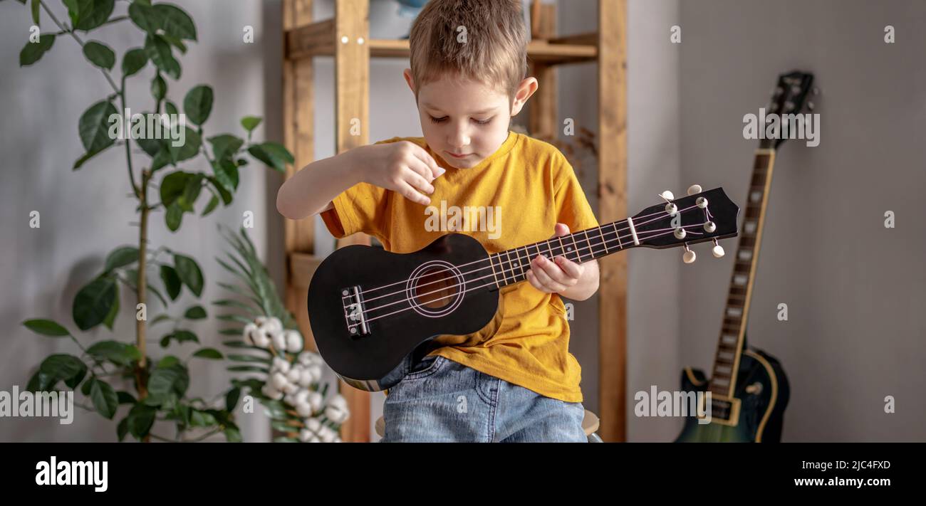 Cute funny boy is playing ukulele guitar in the music room. Joyful ...