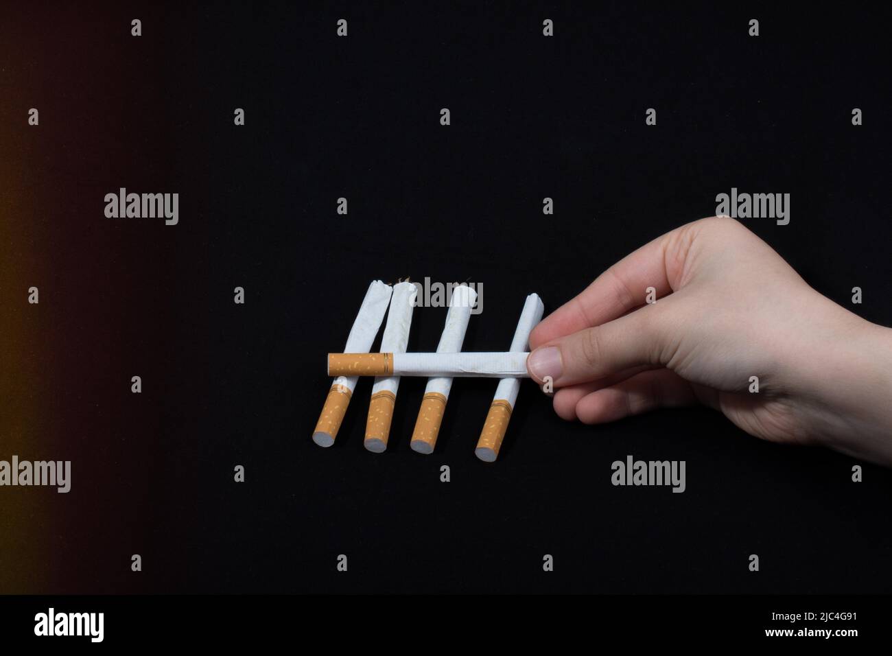 Hand is holding crossed cigarettes on black background Stock Photo - Alamy